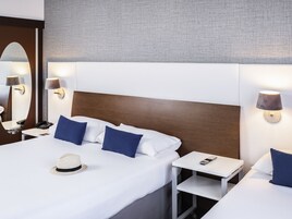 Quarto de hotel com uma cama grande, duas mesas de cabeceira, um criado-mudo, um espelho e uma luminária na parede.