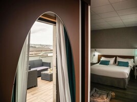 Quarto de hotel com varanda, cama com almofadas, mesa de cabeceira e abajur.