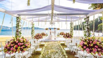 Preparação para uma cerimônia de casamento com um corredor branco, arranjos florais e vista para o mar.
