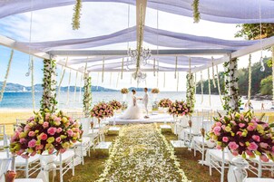 Preparação para uma cerimônia de casamento com um corredor branco, arranjos florais e vista para o mar.