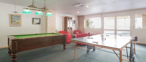 Um quarto com mesa de bilhar, mesa de pingue-pongue e mesa de sinuca.