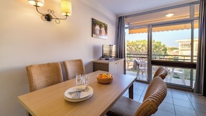 Uma sala de jantar com mesa de madeira, cadeiras de vime, uma cesta de frutas e uma televisão sobre um móvel.