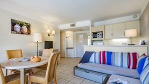 Uma sala de estar moderna com sofá, mesa de jantar e cadeiras. Há uma área de cozinha com armários e micro-ondas.