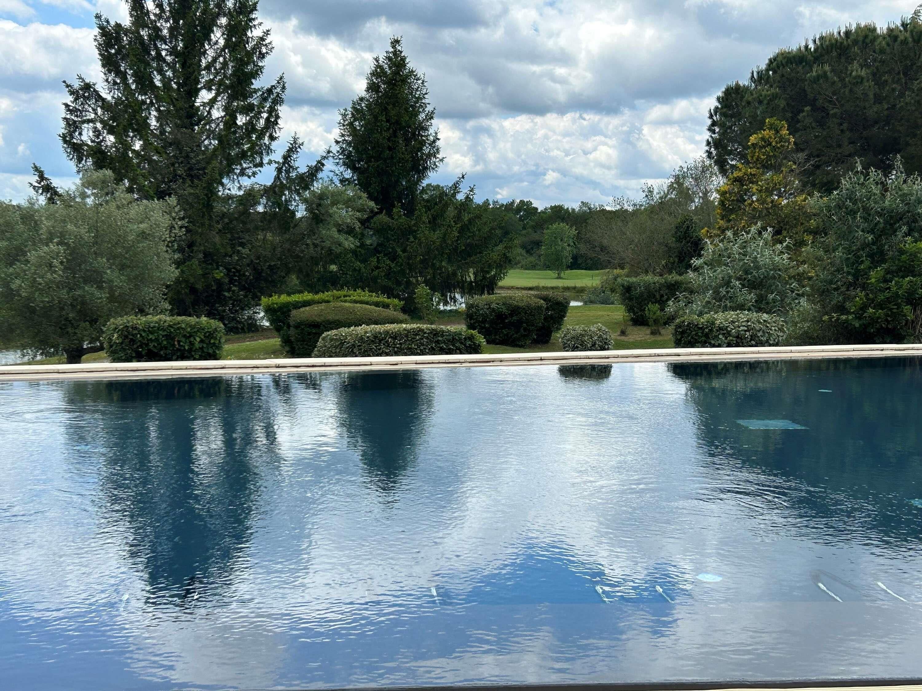 Uma piscina com água cristalina, cercada por sebes e árvores bem cuidadas.