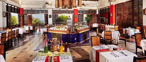 Um restaurante com várias mesas, uma área central de buffet e vista para o exterior.