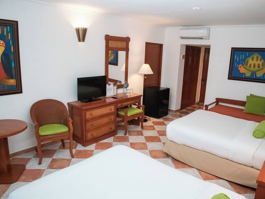 Quarto de hotel com cama, escrivaninha com cadeira, televisão, espelho e um quadro na parede.