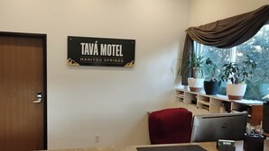 Placa do Tava Motel, um mapa, uma mesa com um computador e plantas em vasos.
