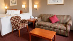 Quarto de hotel com uma cama, um sofá listrado, uma poltrona estampada, uma pequena mesa de madeira e uma mesa de cabeceira com abajur.