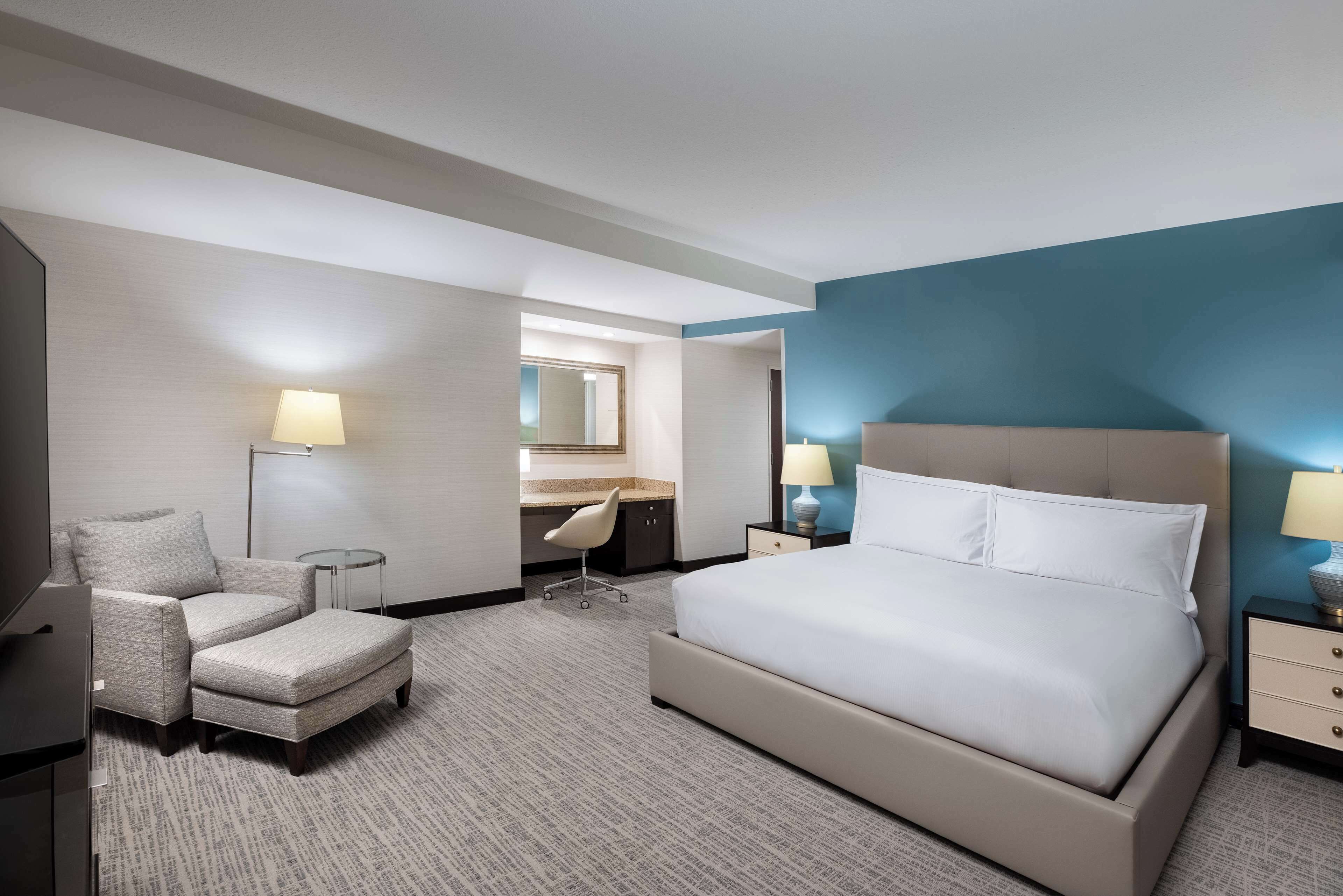 Quarto de hotel com uma cama grande, uma escrivaninha, uma cadeira e uma televisão.