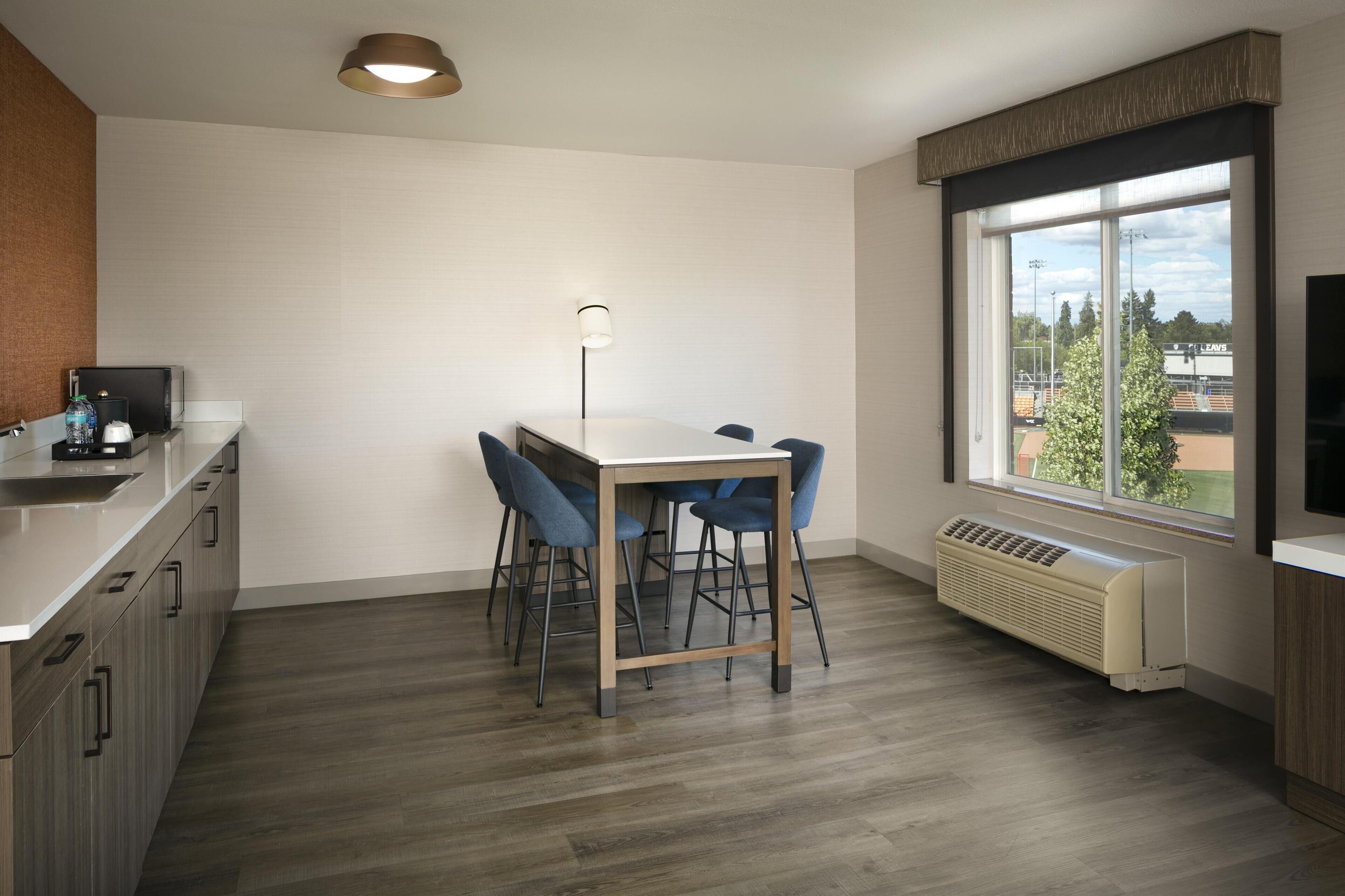 Cozinha moderna com mesa de jantar, cadeiras, fogão embutido e uma grande janela com vista para o exterior.