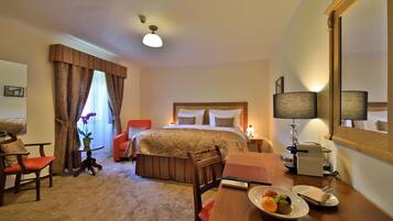 Quarto de hotel com cama, escrivaninha com luminária, cadeira, pequena mesa com um vaso e um espelho grande.