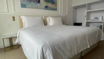 Uma cama grande com roupa de cama branca, uma mesa de cabeceira e um quadro pendurado na parede.