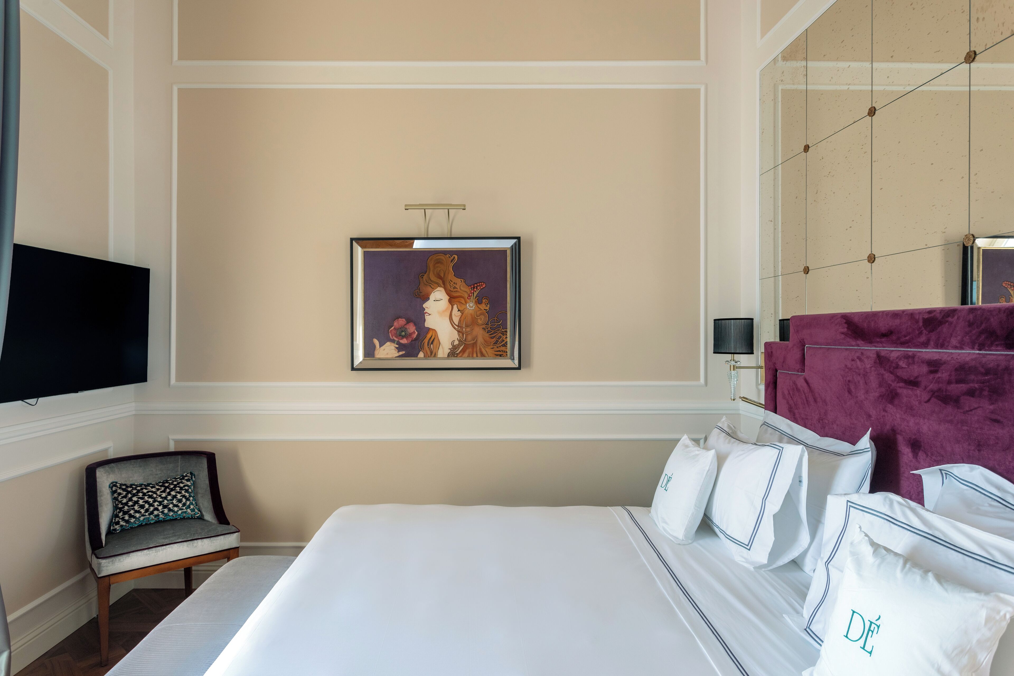 Quarto de hotel com uma cama grande, uma obra de arte emoldurada na parede, uma televisão e uma cabeceira roxa.