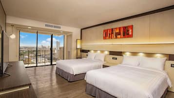 Quarto de hotel com duas camas, uma escrivaninha e uma janela grande com vista para a cidade.