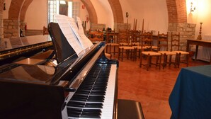 Um piano de cauda em um salão com paredes de tijolos em arco e cadeiras de madeira.
