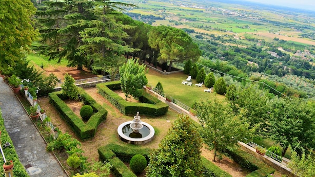 Um jardim exuberante com uma fonte, sebes bem aparadas e uma vista panorâmica do campo.