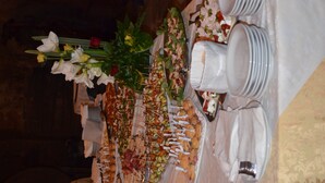 Mesa de buffet com diversos alimentos, incluindo espetinhos e uma arrumação floral.