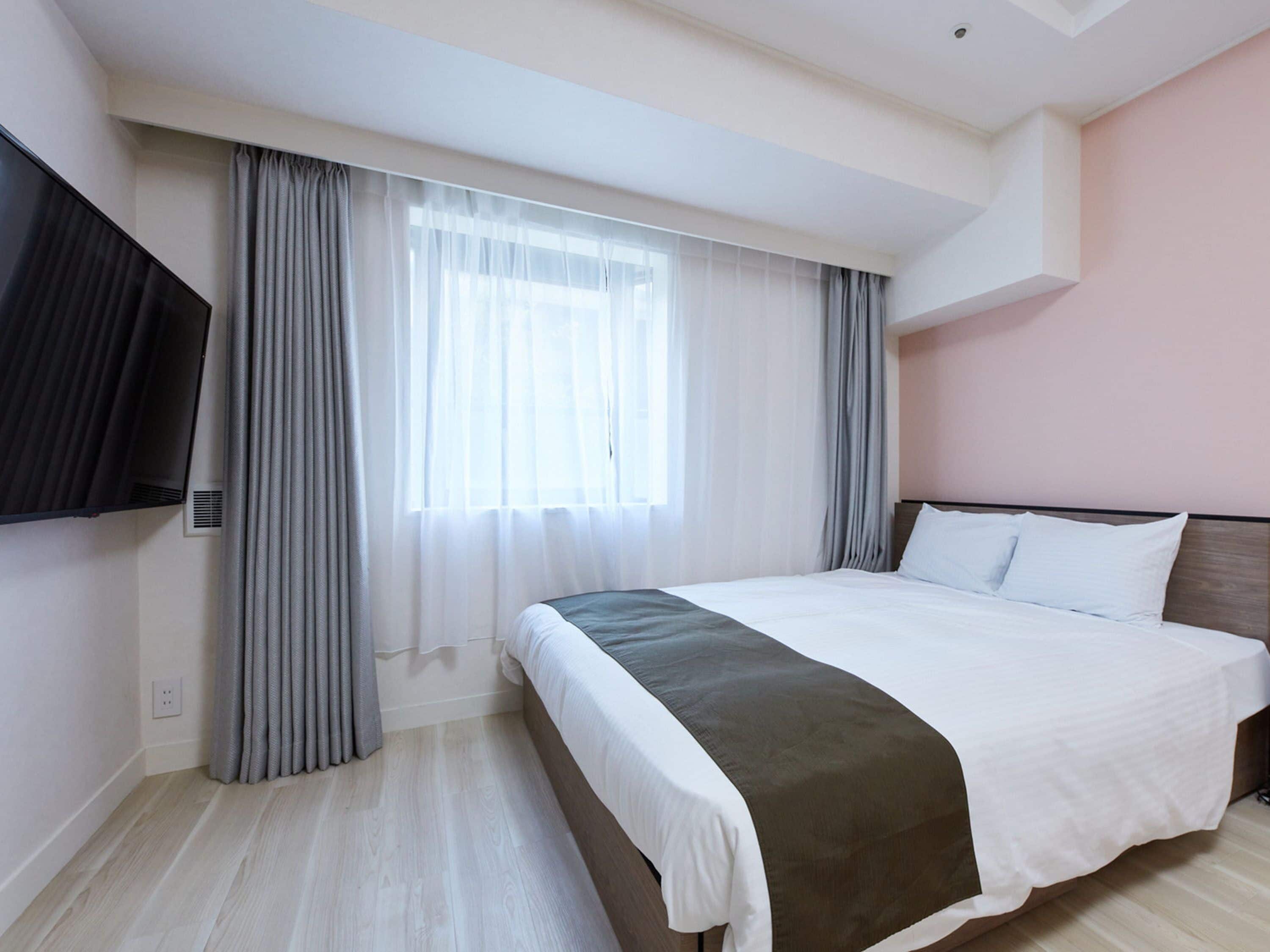 Quarto de hotel com cama grande, televisão de tela plana na parede e janela com cortinas finas.