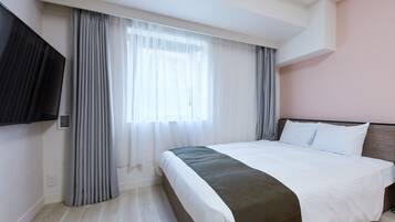 Quarto de hotel com cama grande, televisão de tela plana na parede e janela com cortinas finas.