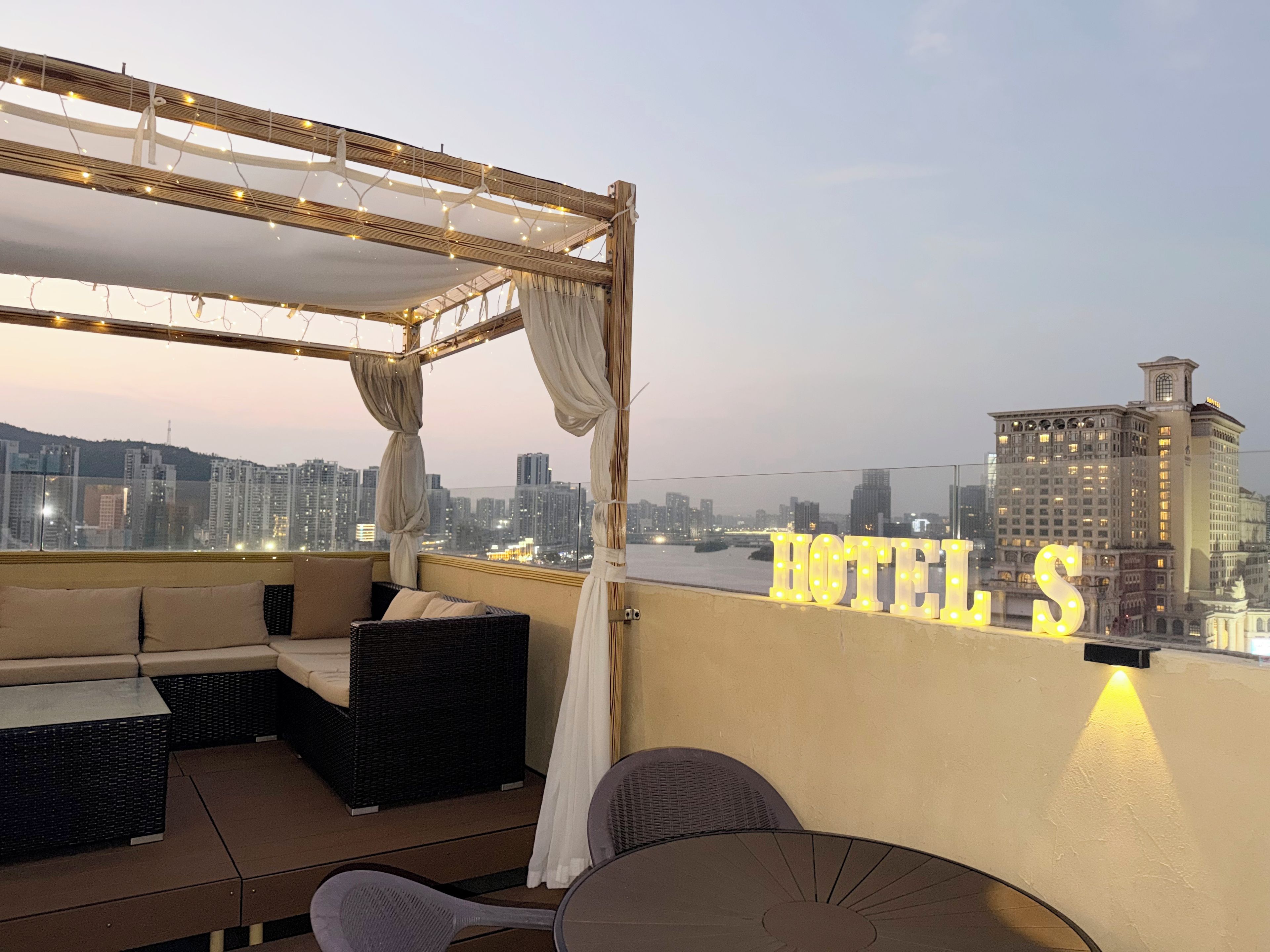 Uma varanda com vista para o horizonte urbano, um toldo com luzes de cordão e uma placa que diz 'HOTELS'.