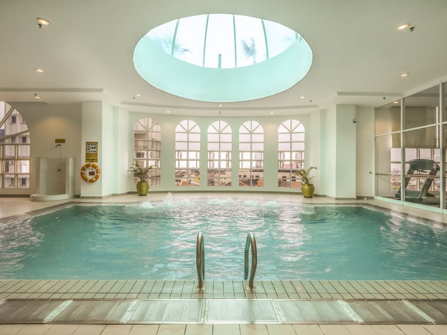 Piscina interior com claraboia, janelas amplas e chão em mosaico.