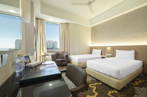 Quarto de hotel com duas camas, uma escrivaninha, uma cadeira, uma luminária de mesa e vista para a cidade.