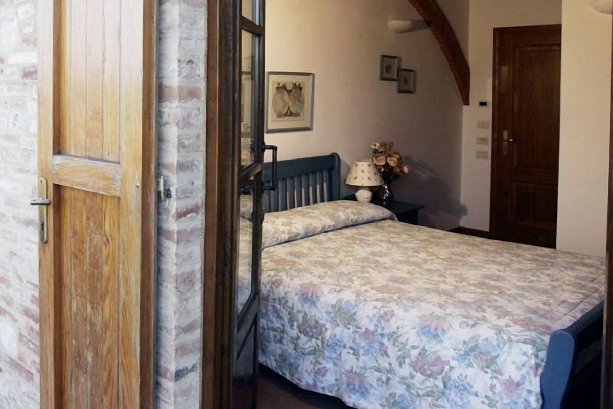 Quarto com cama, porta de madeira, mesa de cabeceira com abajur e parede com quadros.