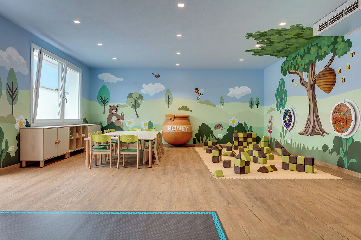 Uma sala de jogos infantil com um grande mural, uma mesa de brincar e um tapete de atividades.