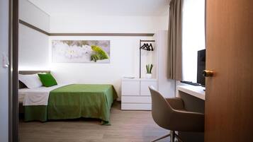 Quarto com cama, escrivaninha, cadeira, televisão e planta fixada na parede.