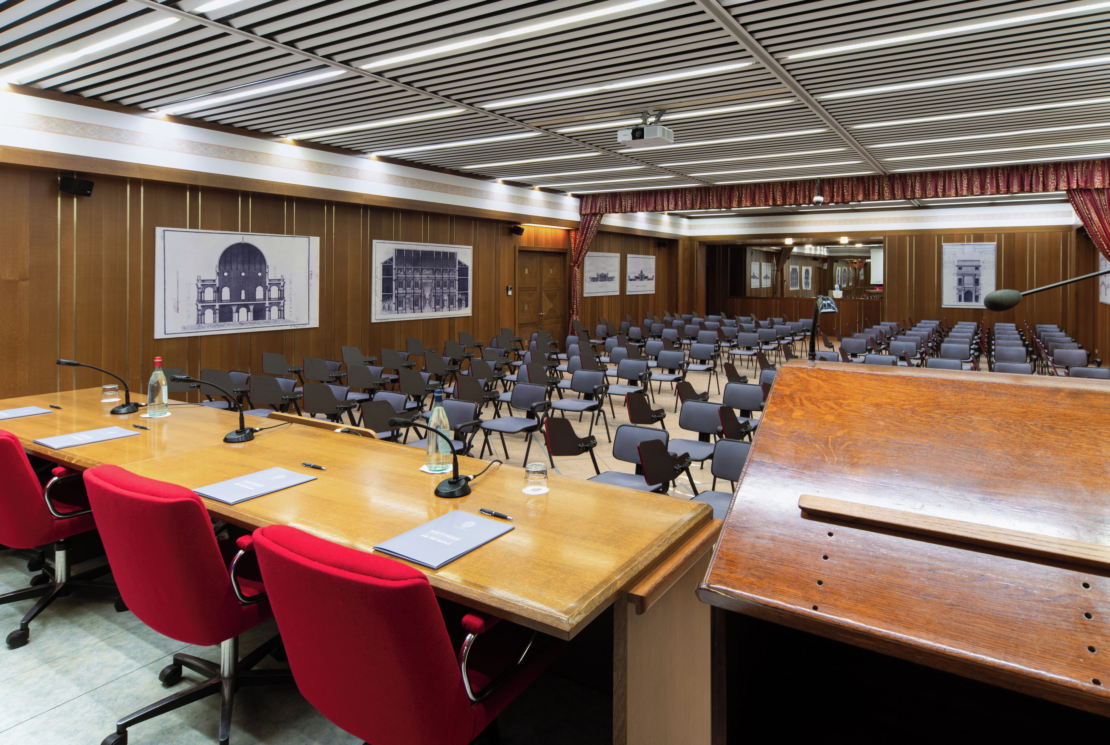 Uma sala de conferências com uma mesa comprida, cadeiras vermelhas e um pódio de madeira.