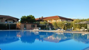 Piscina com espreguiçadeiras e um prédio com telhado vermelho ao fundo.