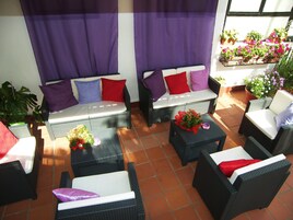 Uma área de pátio com móveis de vime, incluindo sofás e cadeiras, e uma pequena mesa com um arranjo de flores.