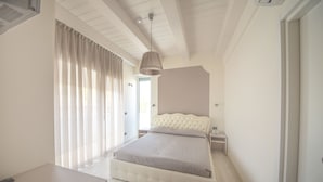 Quarto com cama grande, mesa de cabeceira, luminária pendente e vista para o exterior pela janela.