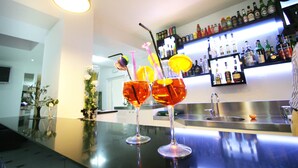 Uma área de bar com dois copos de coquetéis vermelhos, variedade de garrafas em prateleiras e design de interiores moderno.