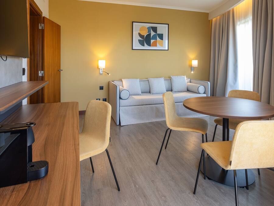 Quarto de hotel moderno com uma escrivaninha de madeira, um sofá e uma mesa de jantar redonda.