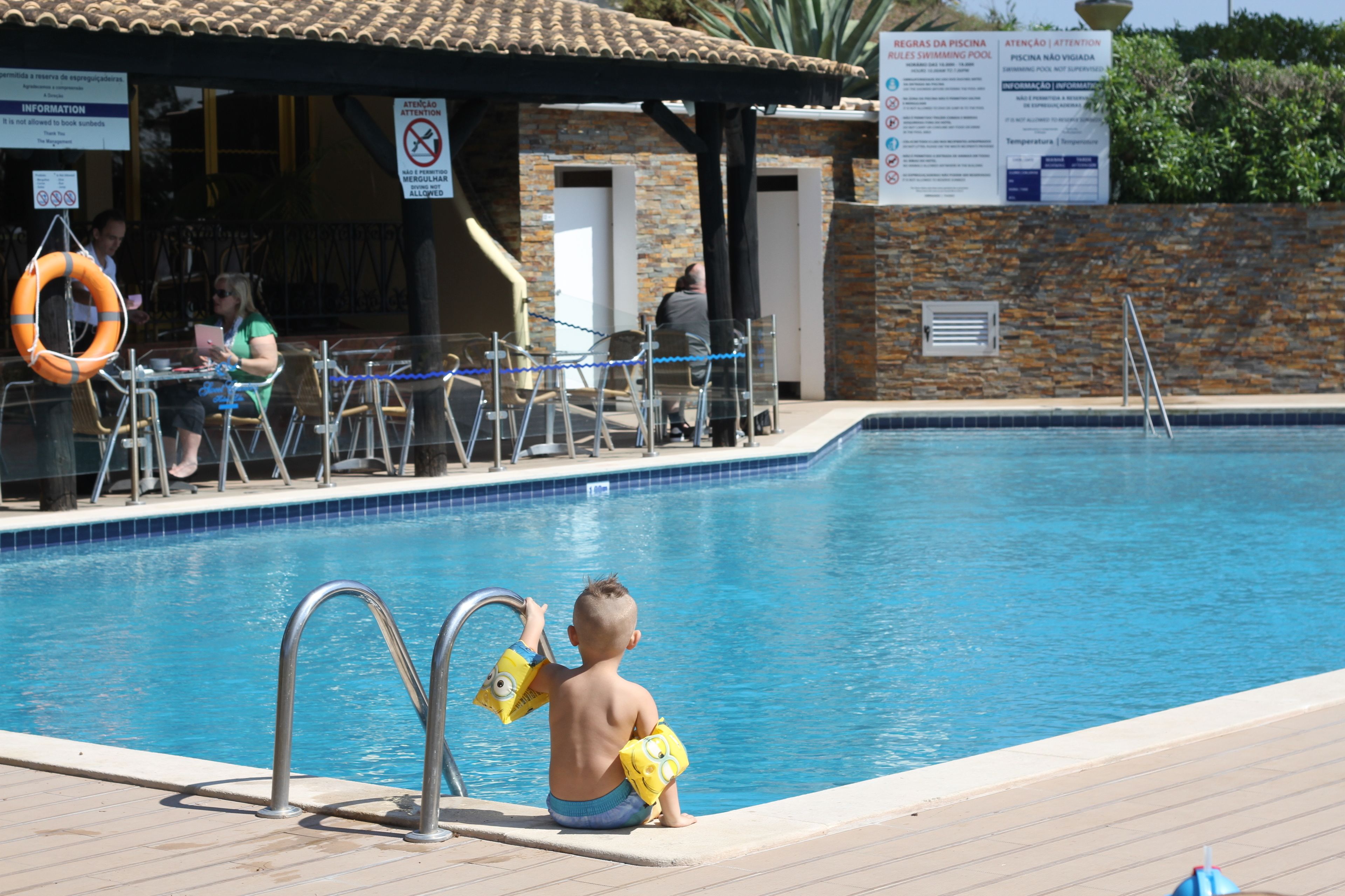 Uma área de piscina com um salva-vidas, um espaço coberto para sentar e um aviso com as regras da piscina.