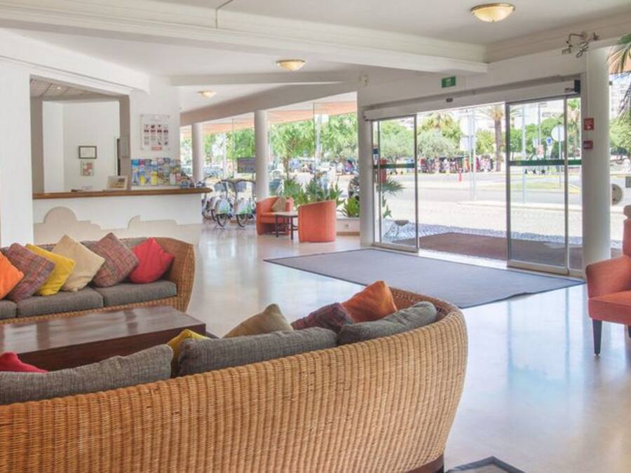 Um hall amplo com sofás de vime, um balcão de recepção e grandes janelas com vista para a rua.