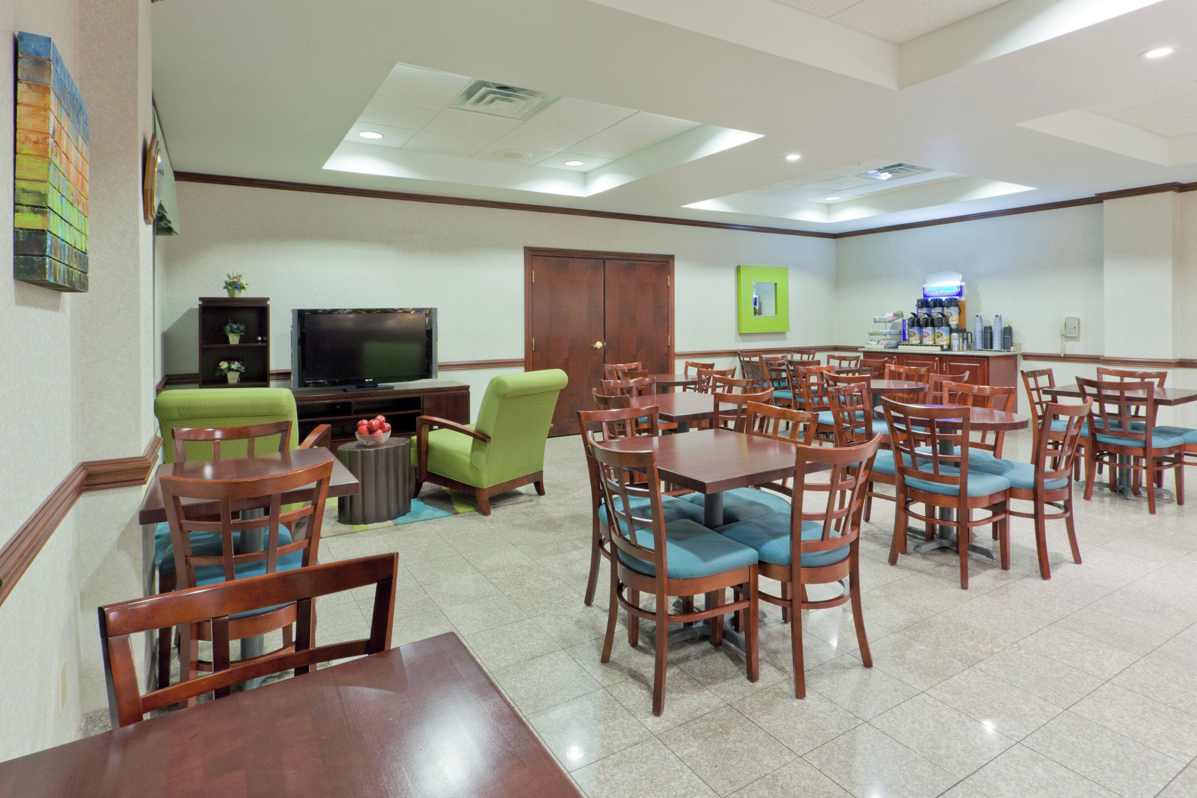 Uma área de refeições de hotel com várias mesas e cadeiras de madeira, uma televisão e um canto com café.