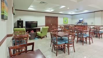 Uma área de refeições de hotel com várias mesas e cadeiras de madeira, uma televisão e um canto com café.