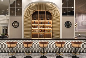 Uma área de bar com uma estante de madeira exibindo garrafas, bancada de mármore e banquetas de vime.