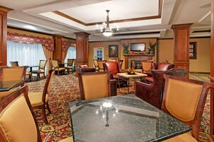 Um hall de hotel com um candelabro, poltronas de couro, lareira e uma televisão.
