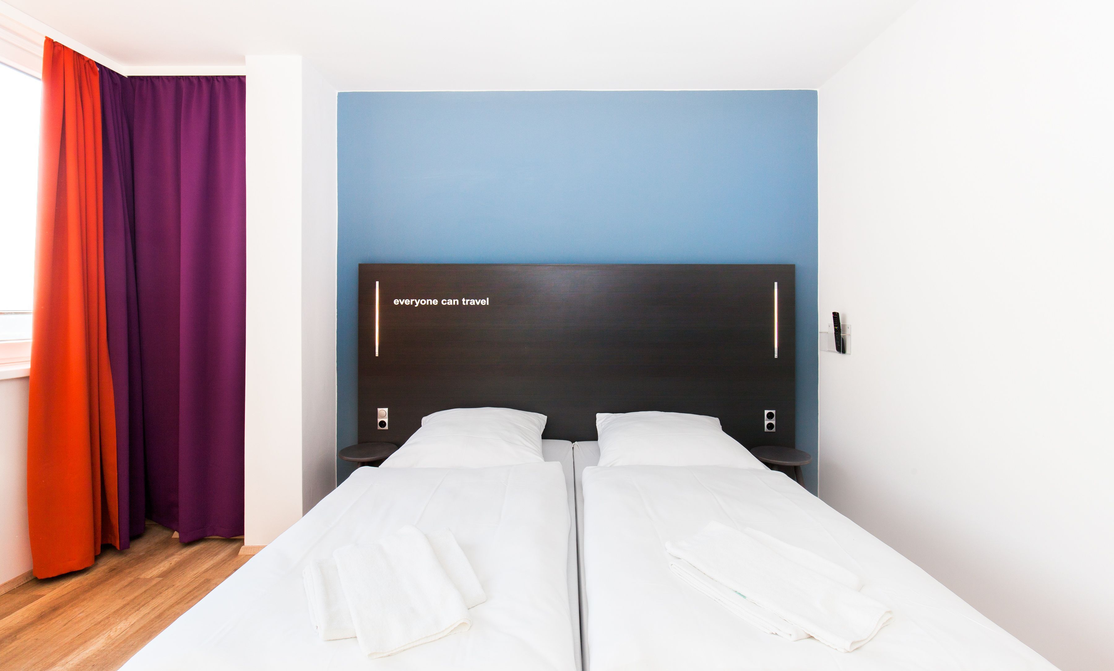 Uma cama de casal com cabeceira escura e parede azul ao fundo.