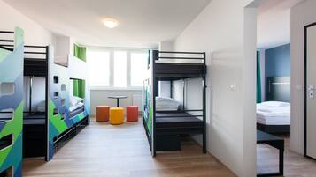Um quarto de dormitório com beliches, uma mesinha e banquinhos coloridos.