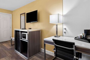 Quarto de hotel com escrivaninha, cadeira, televisão e minibar.