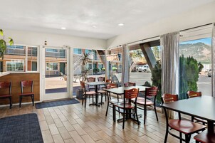 Restaurante com vista para uma montanha, piso de madeira e cadeiras em tons de vermelho e preto.