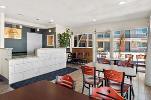 Uma área de recepção de hotel com balcão de mármore, uma placa com a inscrição 'Americas Best Value Inn & Suites' e vista para a área externa com mesas e cadeiras.