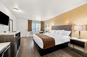 Quarto de hotel com cama, mesa de cabeceira, luminária, televisão e escrivaninha com cadeira.