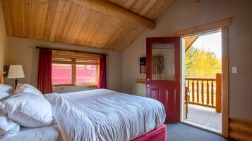 Quarto com teto de madeira, porta vermelha, janela com cortinas vermelhas e vista para um deck de madeira.