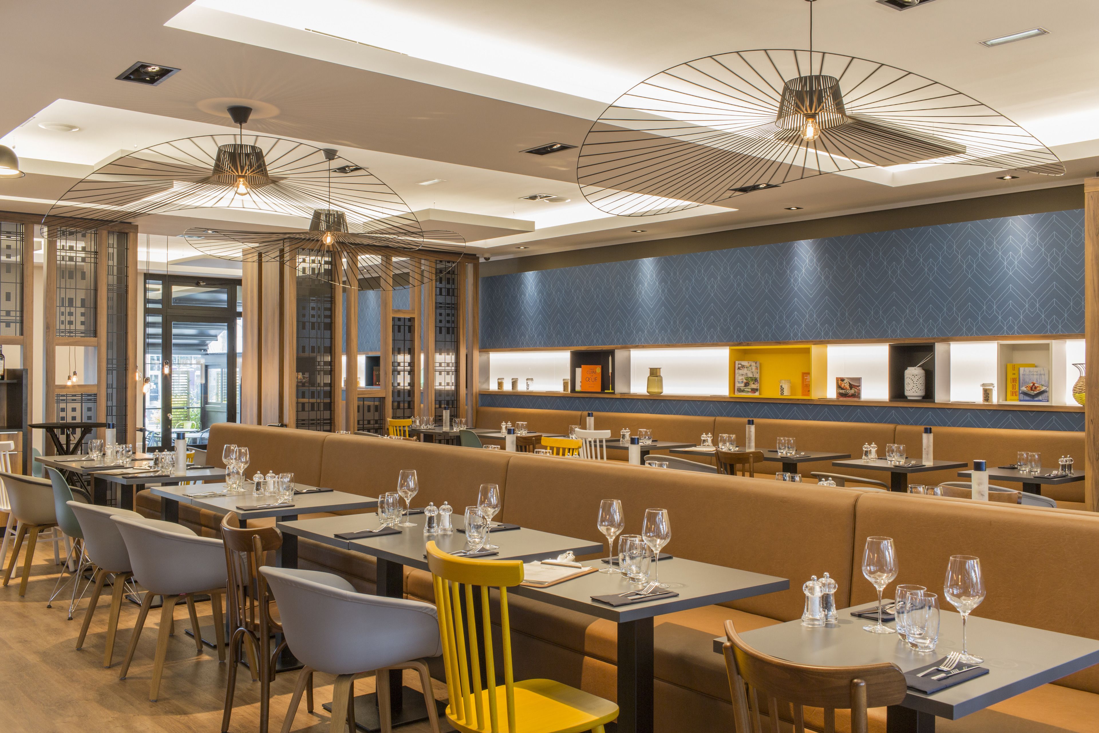Um restaurante moderno com mesas altas e cabines, iluminação pendente e parede com padrão azul.