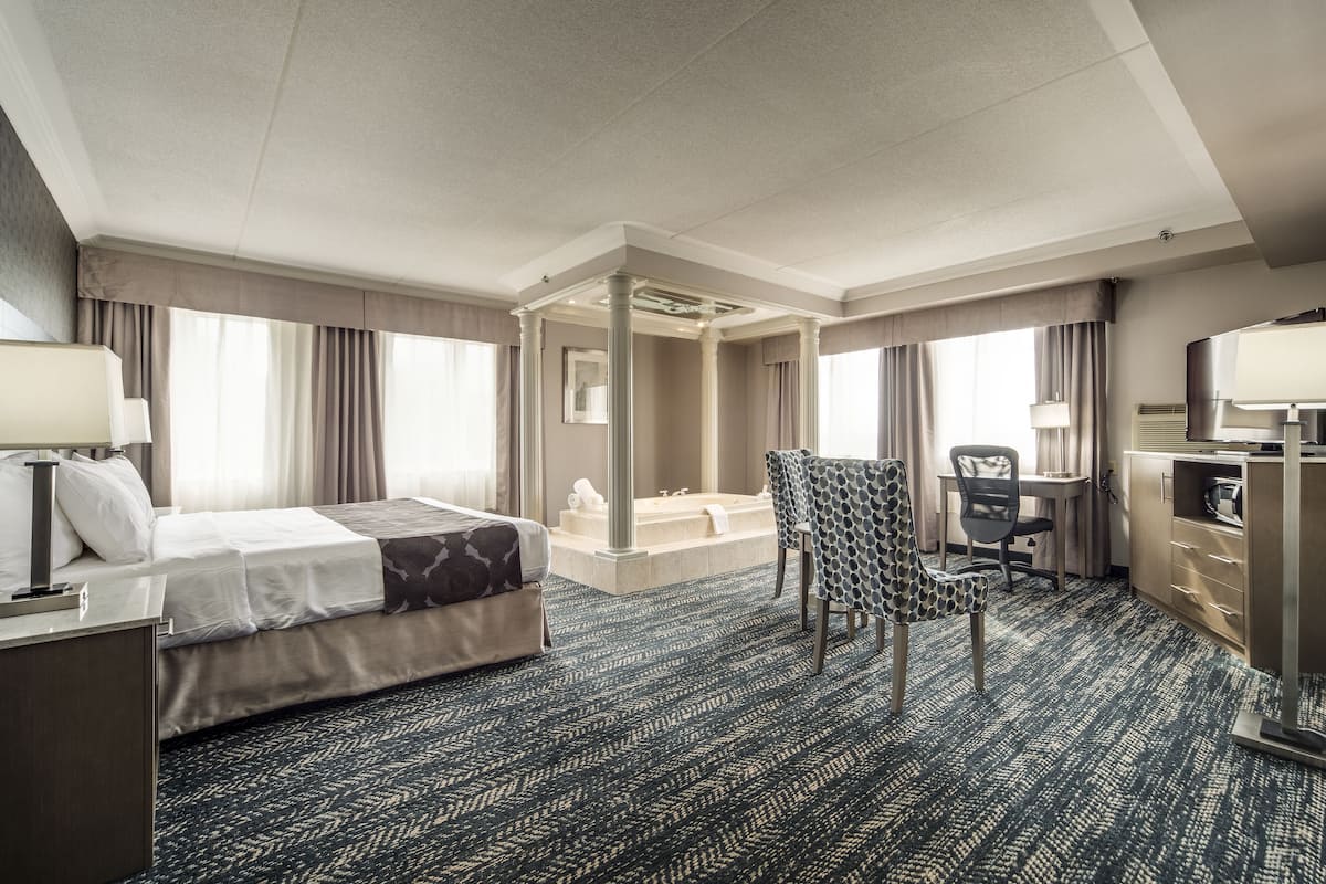 Quarto de hotel com cama, escrivaninha, cadeira e banheiro com banheira.